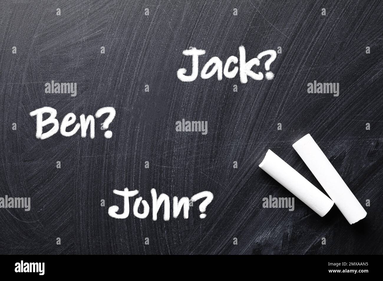Pieces of white chalk and different baby names written on blackboard ...