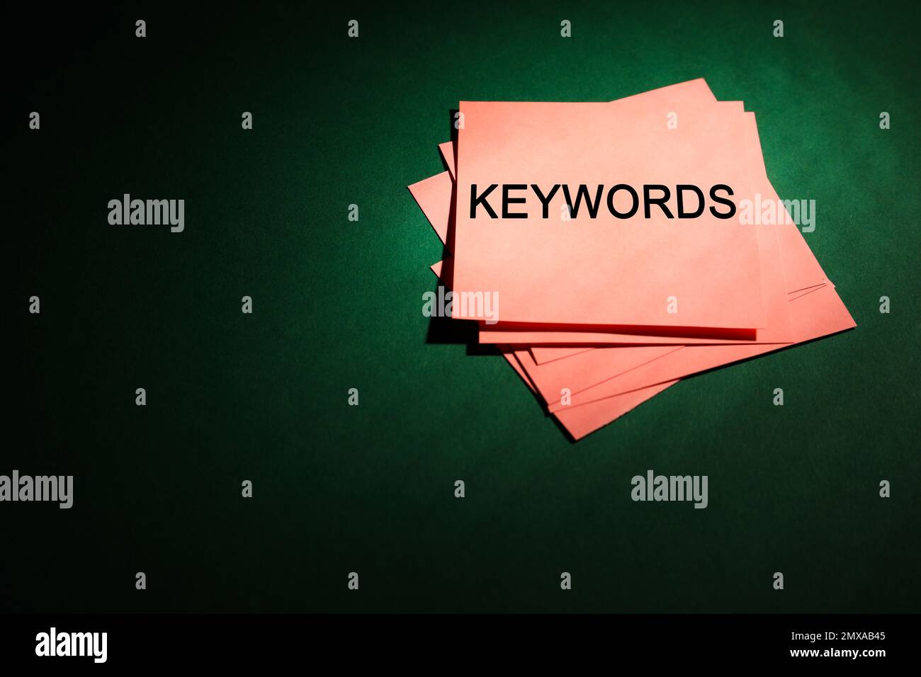 Pink paper card with phrase KEYWORDS on dark green background, above ...