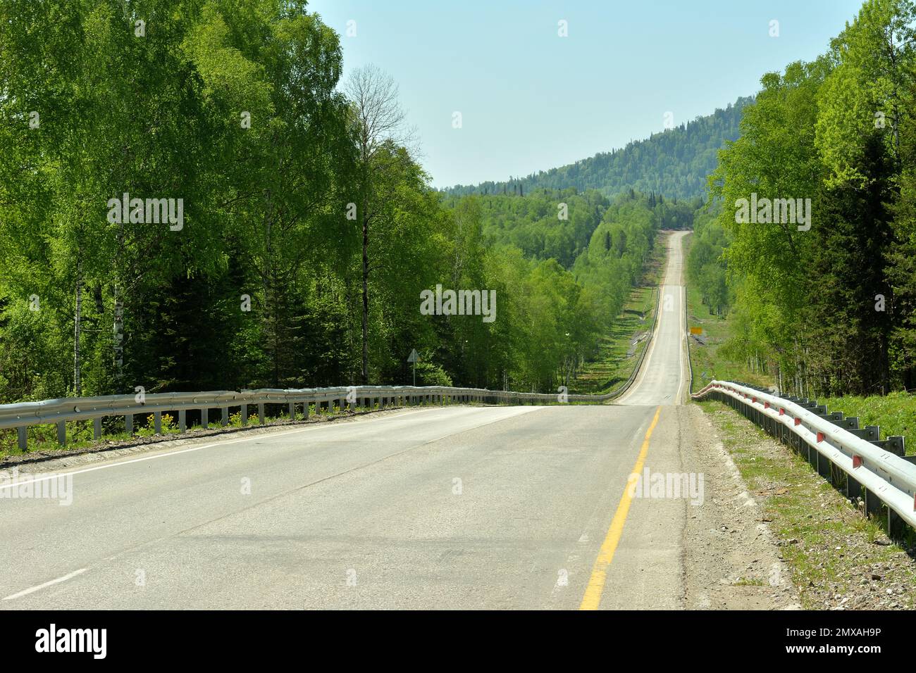 A straight two-lane road with fences descends into the log and rises ...