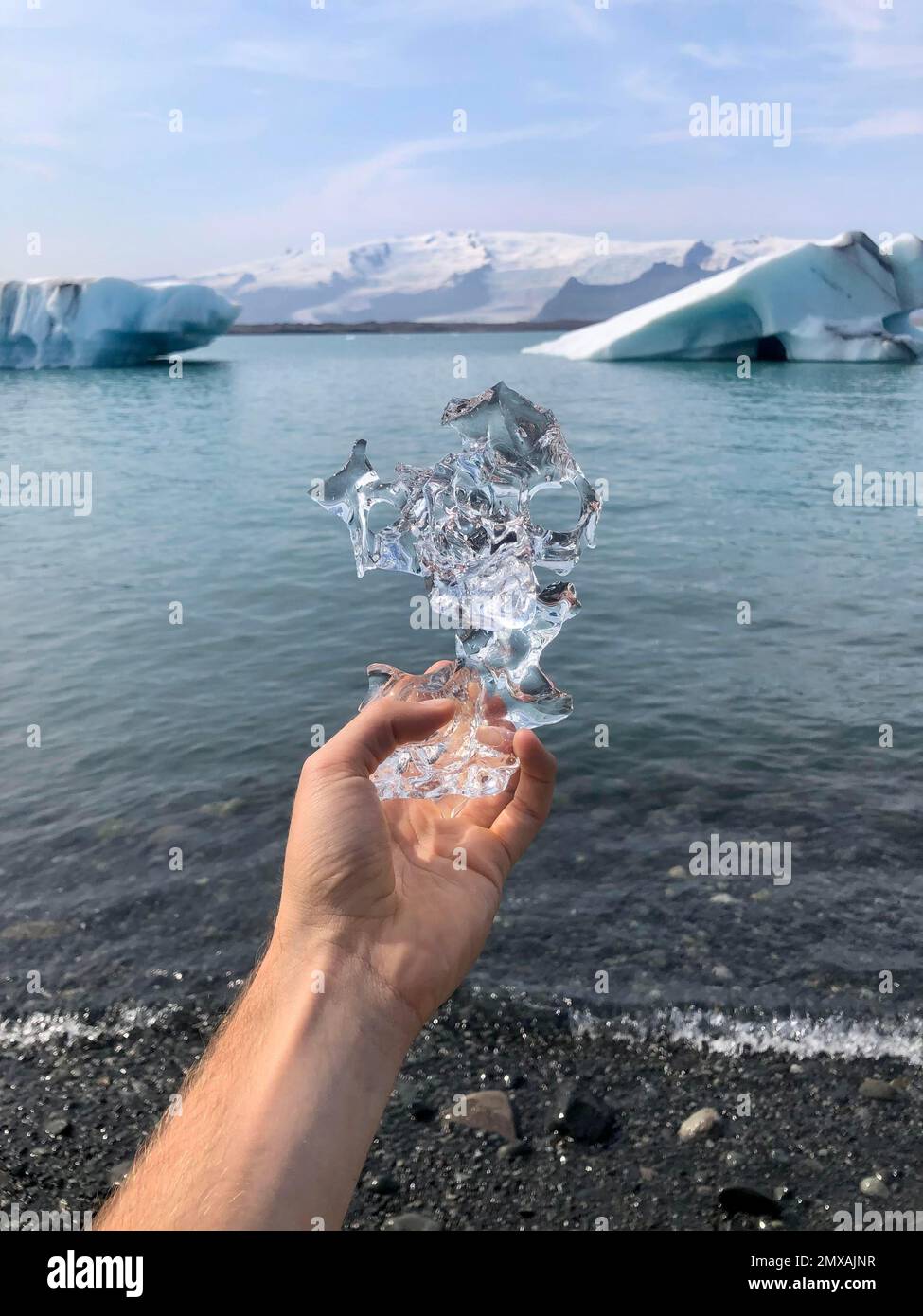 Hand holding ice, behind ice floes on the glacier lagoon, Joekulsarlon ...