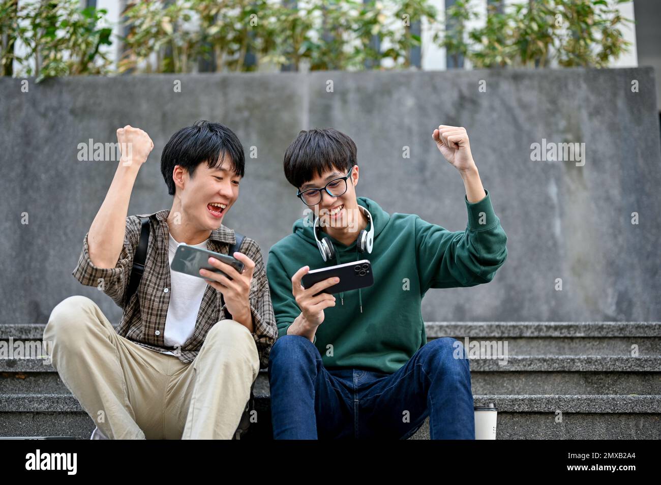 Overjoyed and cheerful young Asian man sits on street stairs watching ...