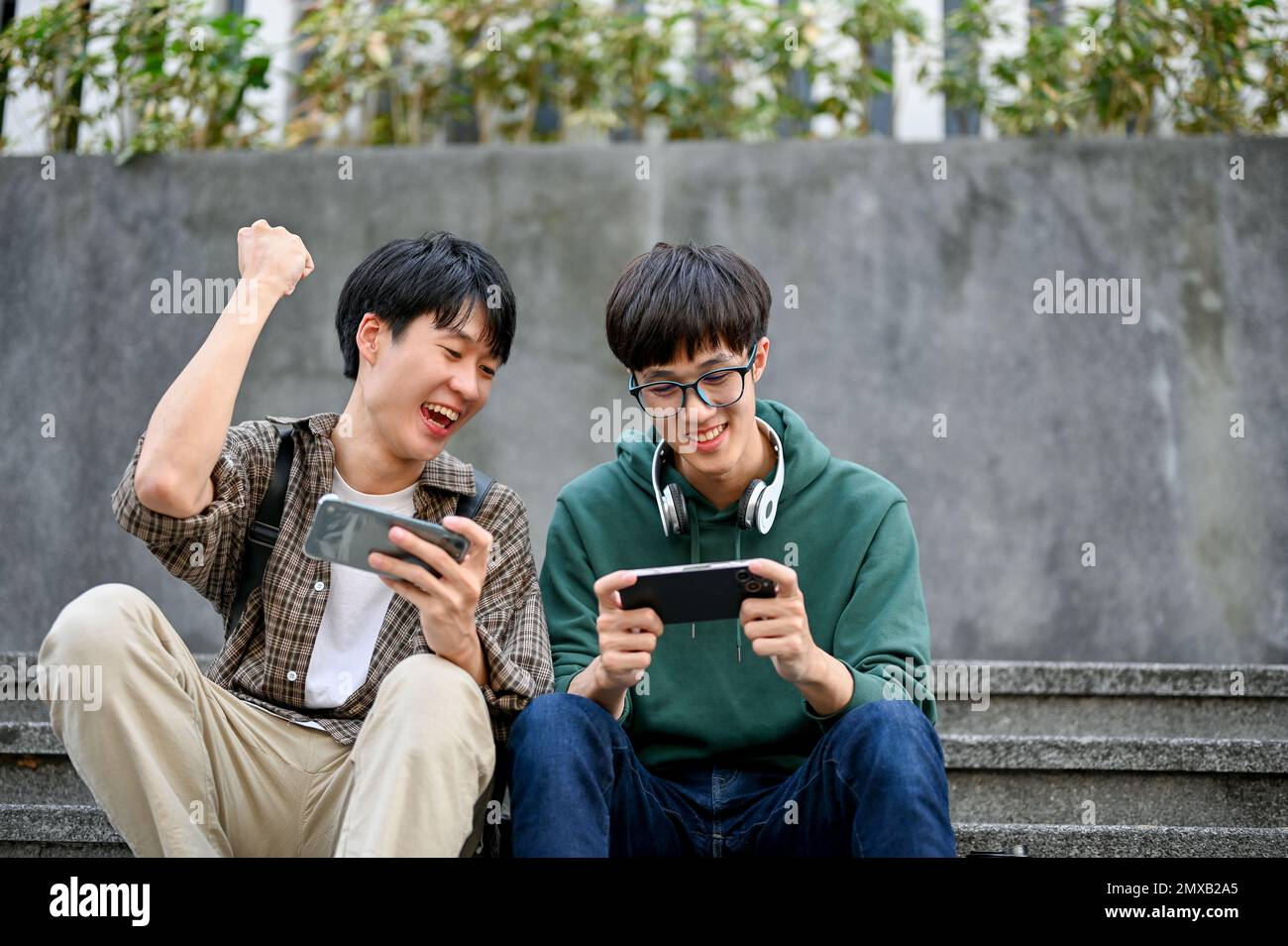 Cheerful and overjoyed young Asian male college student playing mobile ...