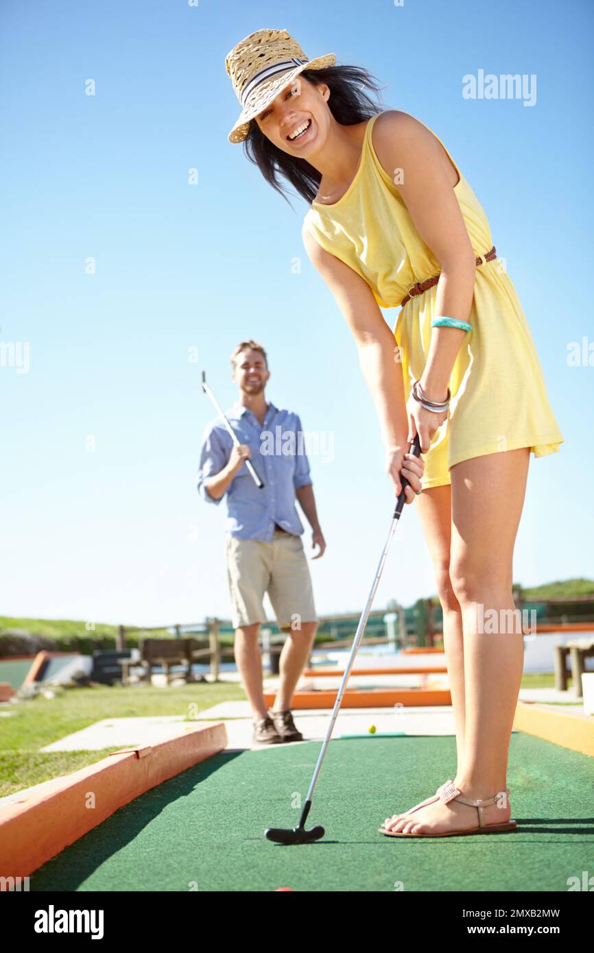 Couple, mini golf and happy woman with club, smile and hit ball on date ...