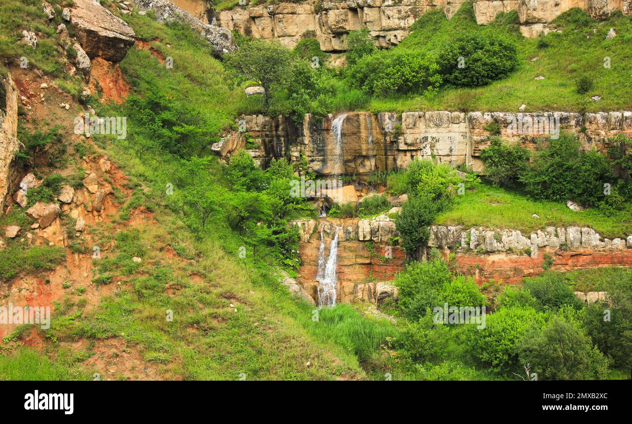 Beautiful waterfall with red mountains in the gorge. The road to the ...