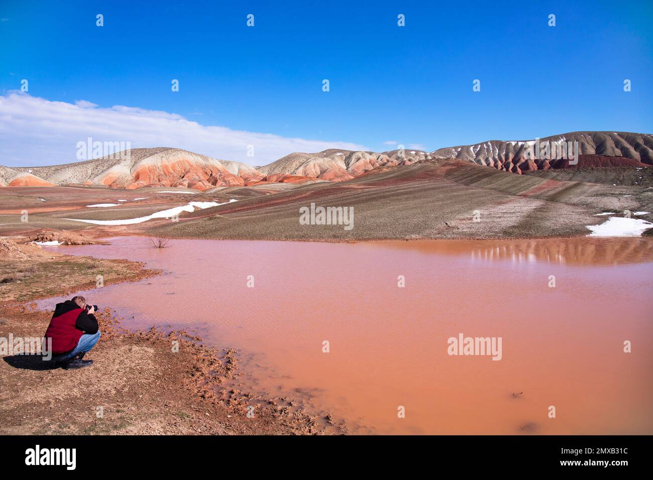A photographer photographs a body of water next to the red mountains ...