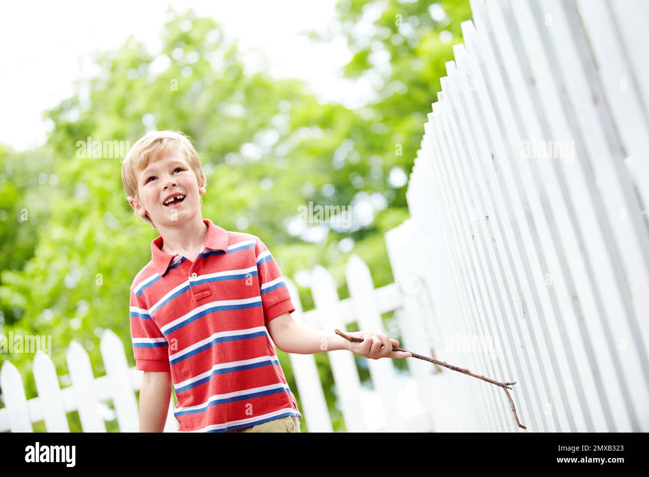 His imagination knows no bounds. A cute young boy running a stick along ...