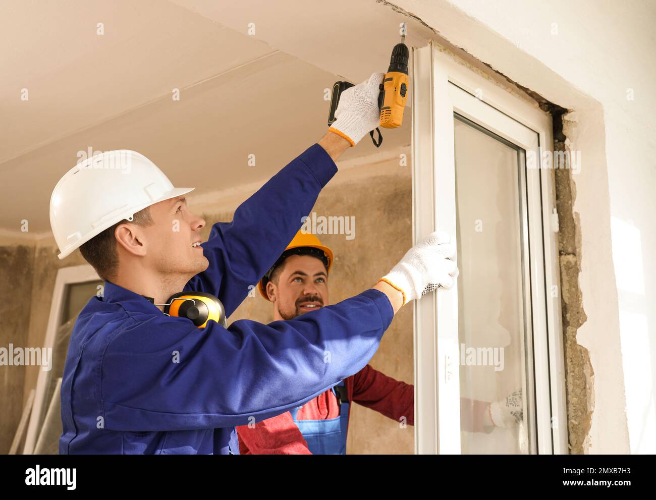 Workers using electric screwdriver for window installation indoors ...
