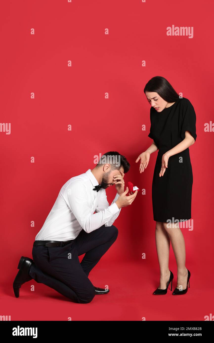 Young woman rejecting engagement ring from boyfriend on red background ...