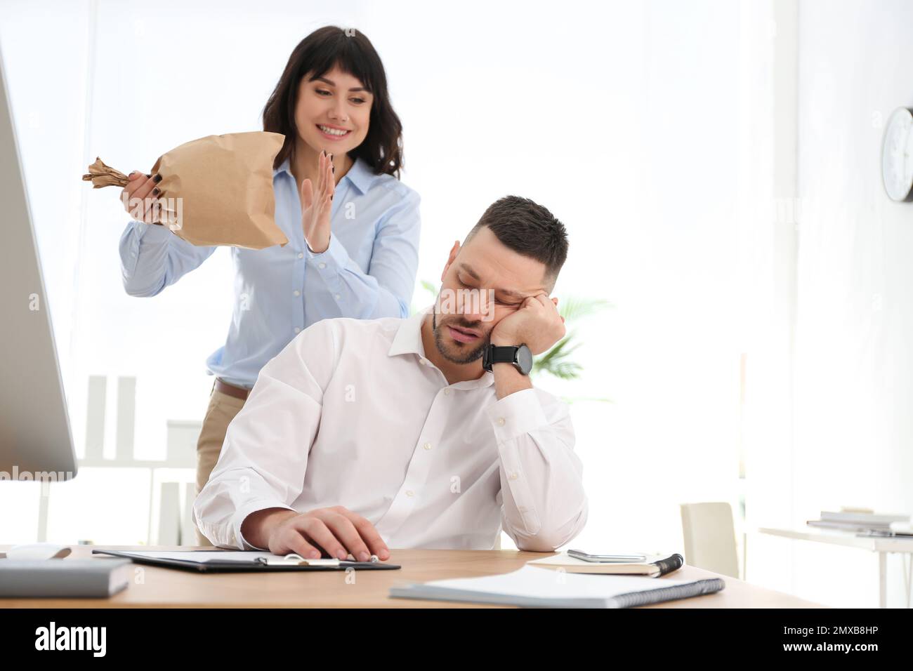 Young woman popping paper bag behind her sleeping colleague in office ...