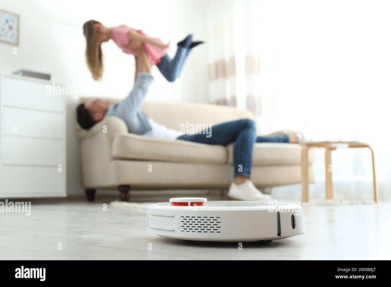 Man and his daughter having fun while robotic vacuum cleaner doing its ...