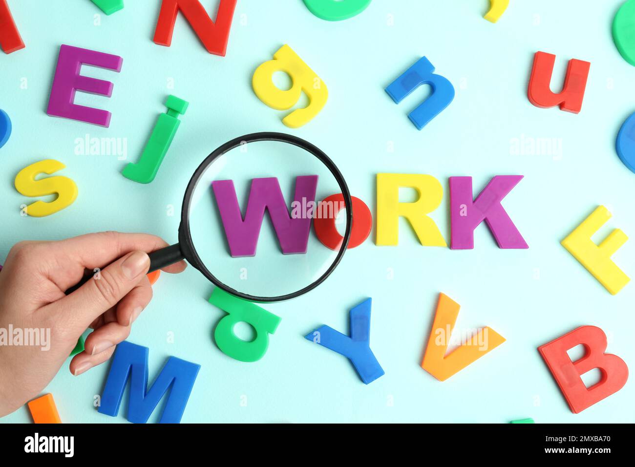 Woman holding magnifying glass over word WORK made with magnet letters ...