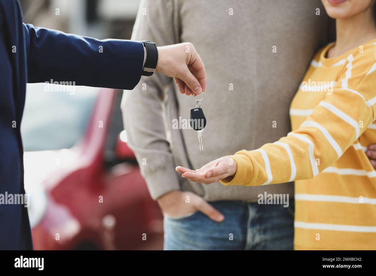 Salesman giving key to customers in modern auto dealership, closeup ...