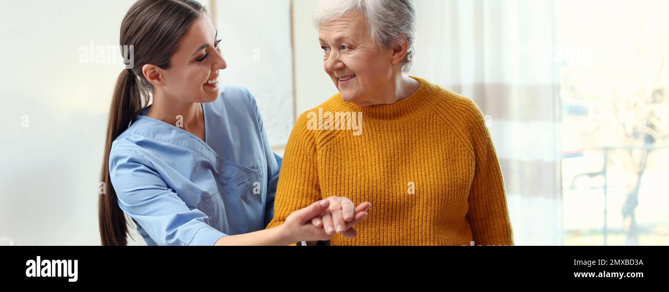 Care worker helping elderly woman to walk in geriatric hospice. Banner ...