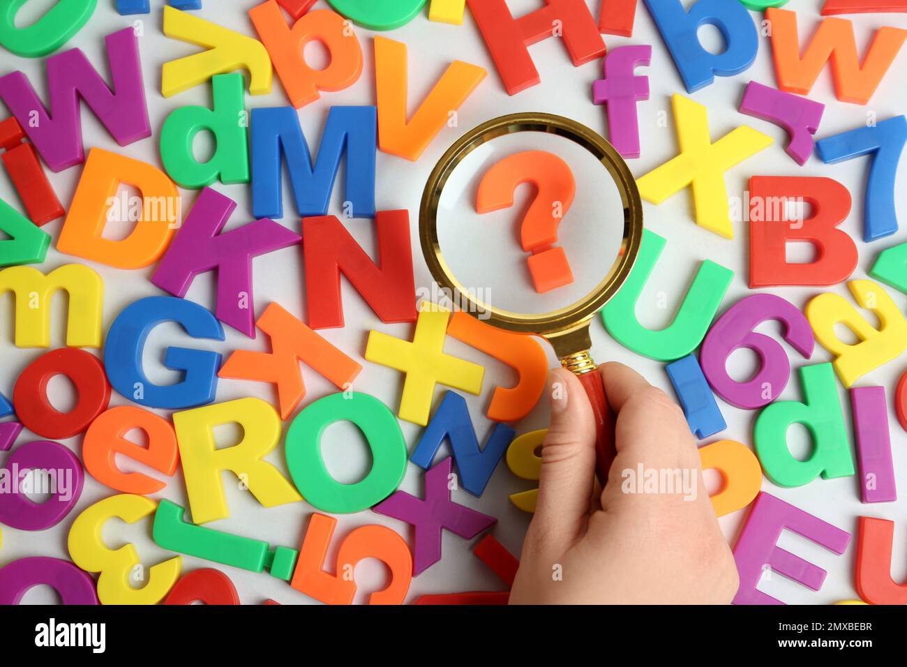 Woman holding magnifying glass over question mark surrounded by magnet ...
