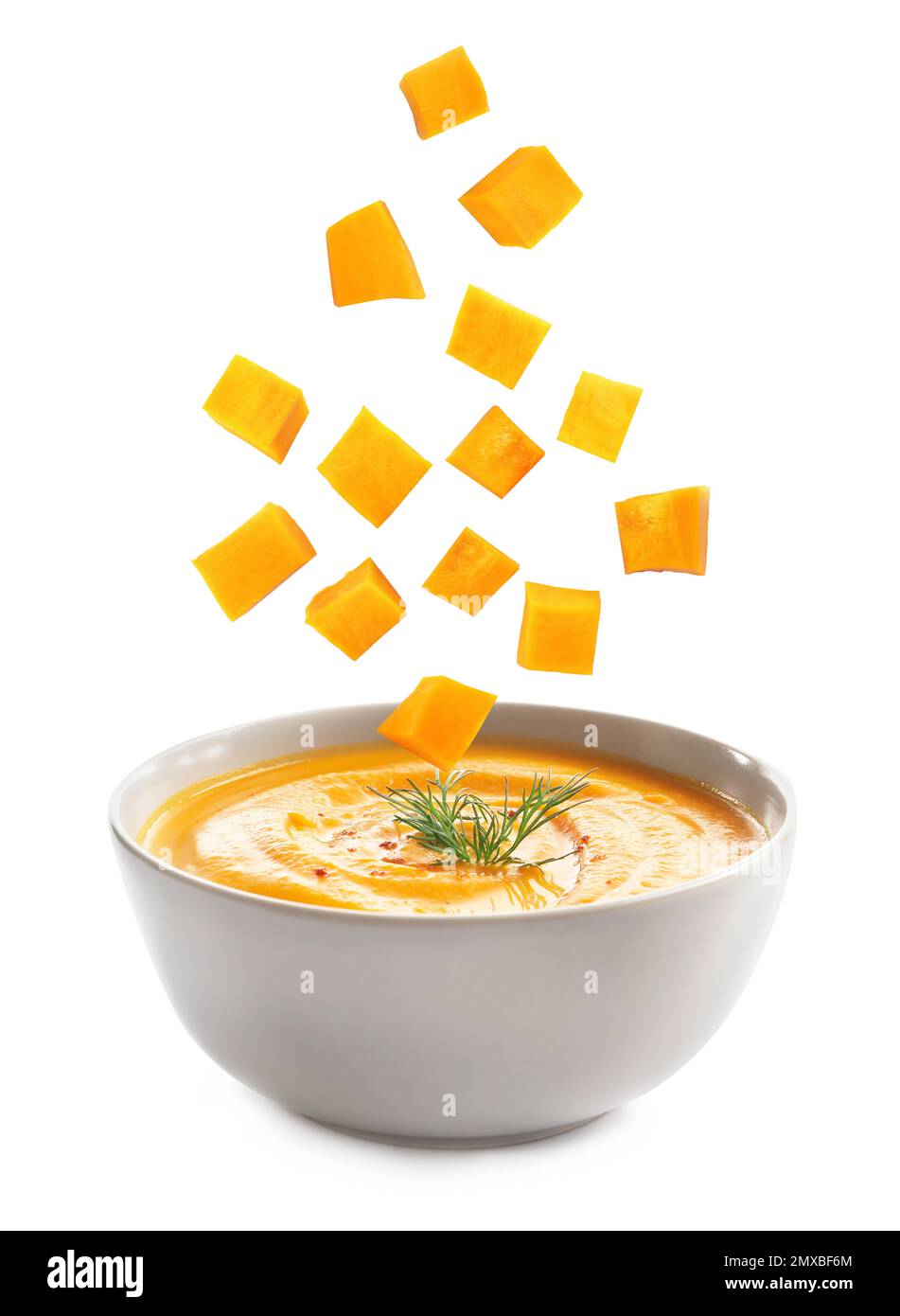 Many pumpkin pieces falling into bowl of homemade soup on white ...