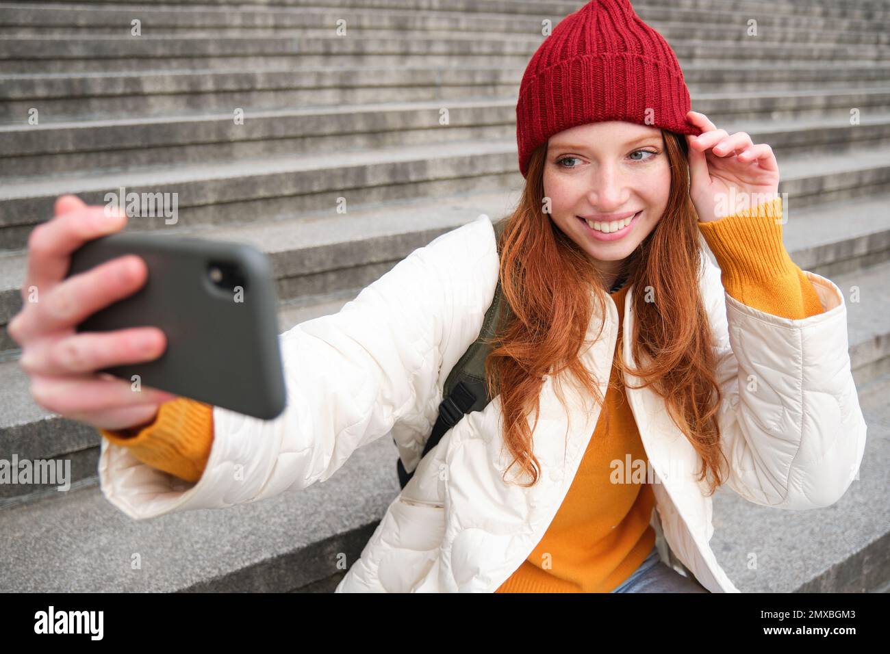 Stylish young girl in red hat, takes photos on smartphone camera, makes ...
