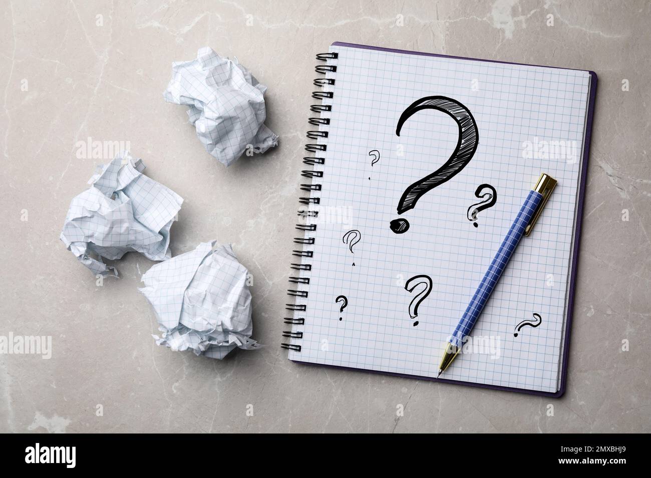 Notebook with question marks, pen and crumpled paper balls on grey ...