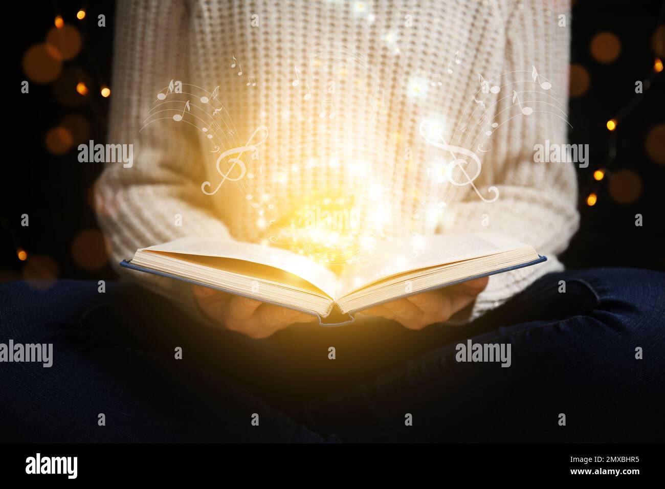 Young woman holding open book with musical notes against dark ...