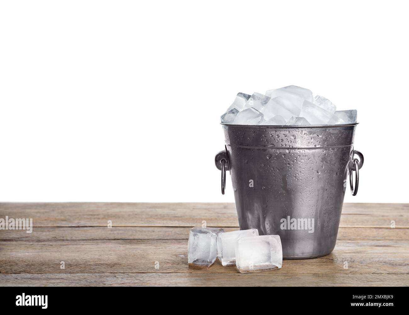 Metal bucket with ice cubes on wooden table against white background ...