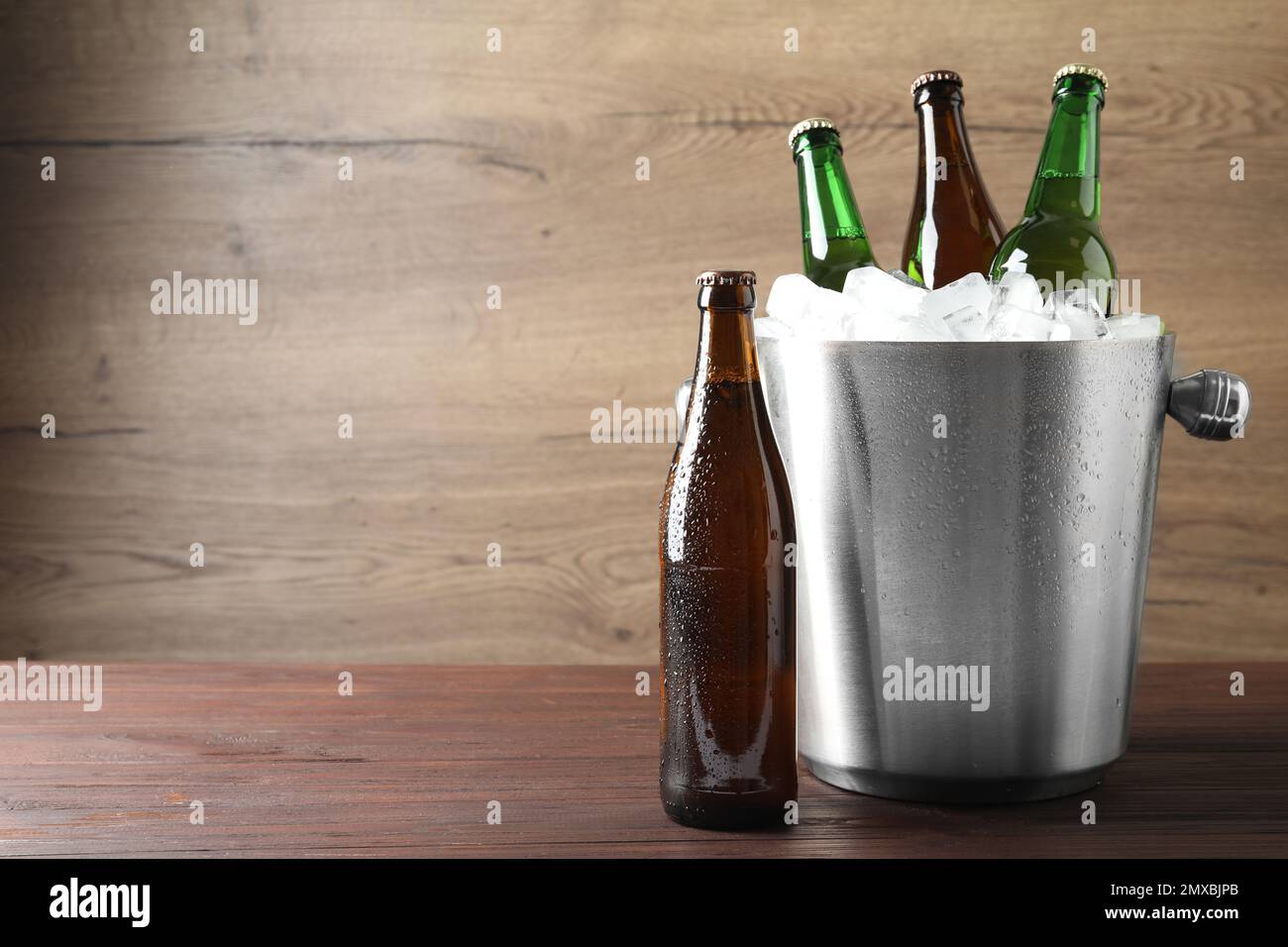 Metal bucket with beer and ice cubes on wooden table. Space for text ...