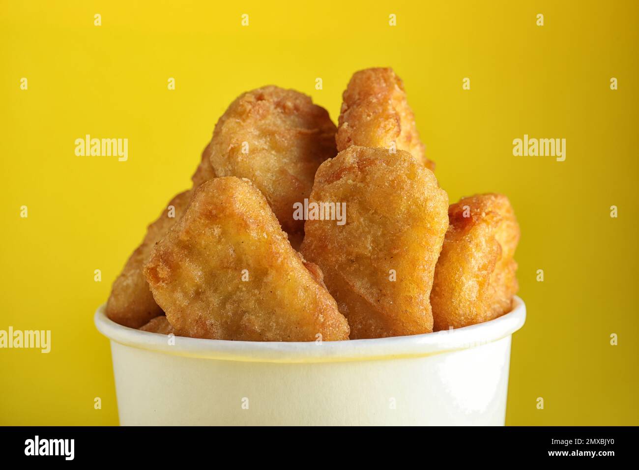 Bucket with tasty chicken nuggets on yellow background, closeup Stock ...