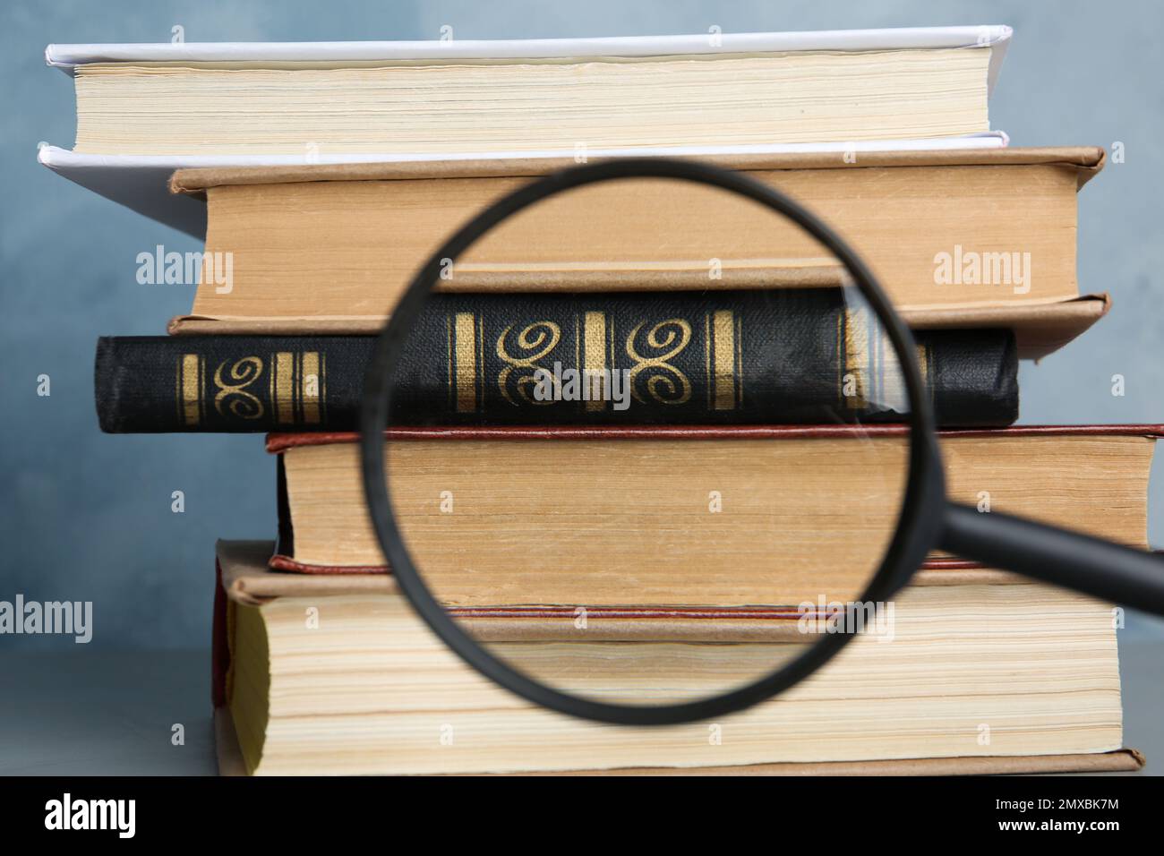 Looking through magnifying glass at stack of vintage books on grey ...