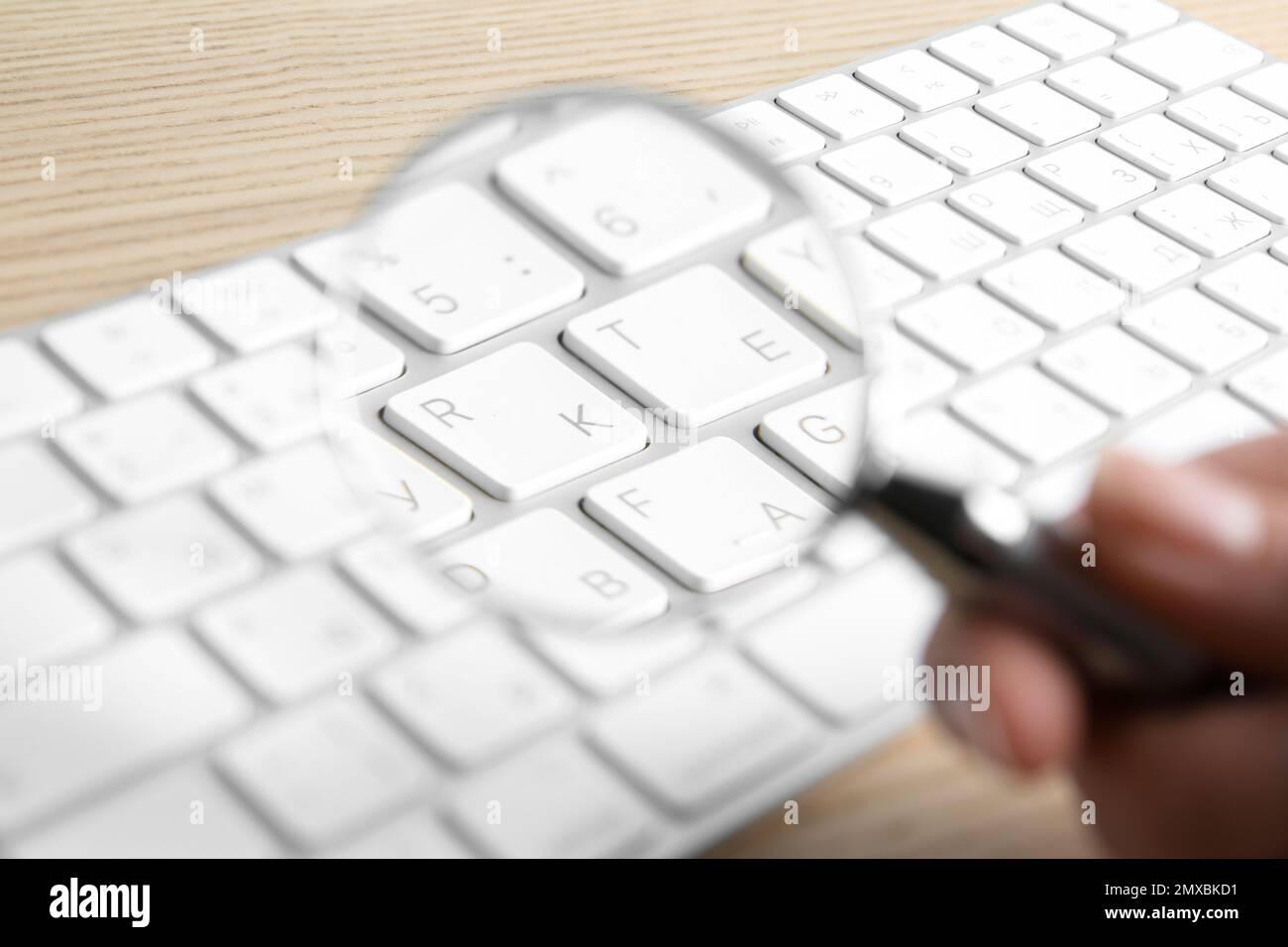 Woman looking through magnifying glass at computer keyboard on table ...