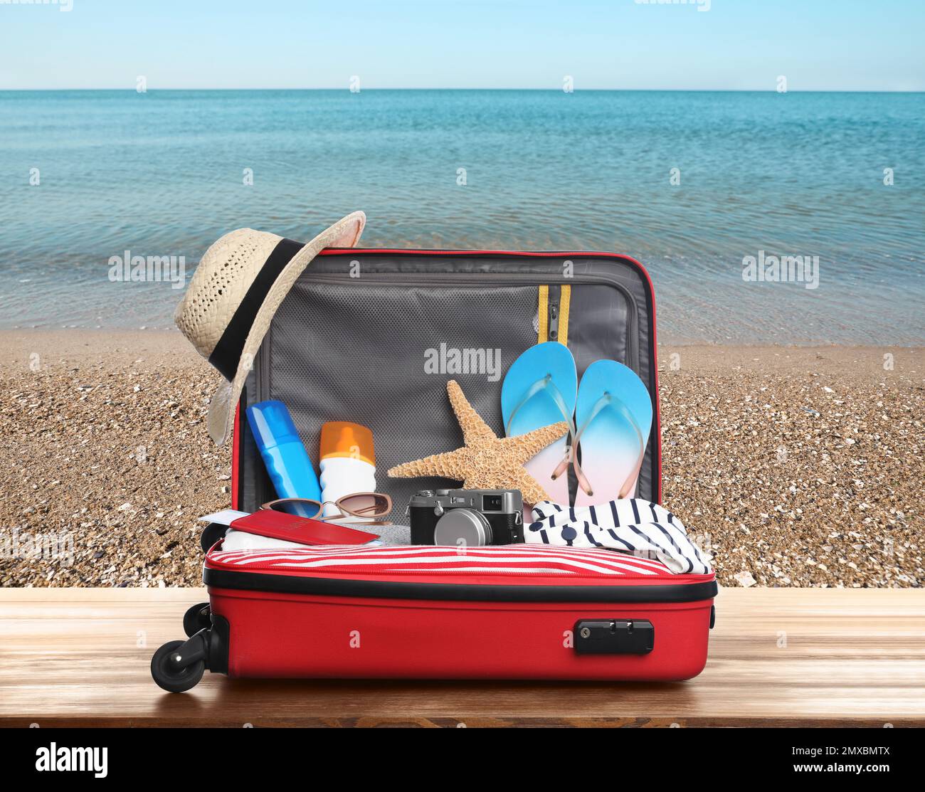 Suitcase with different beach objects on wooden table near sea Stock ...