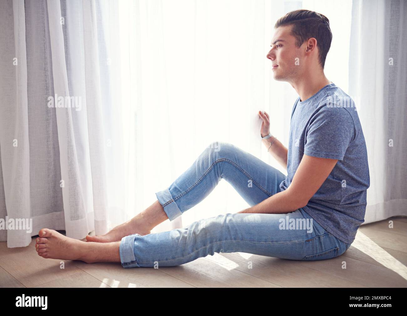 Waiting by the window. a young man sitting on the floor and looking thoughtful by a window Stock ...