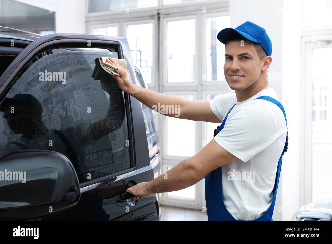 Worker washing tinted car window in workshop Stock Photo - Alamy