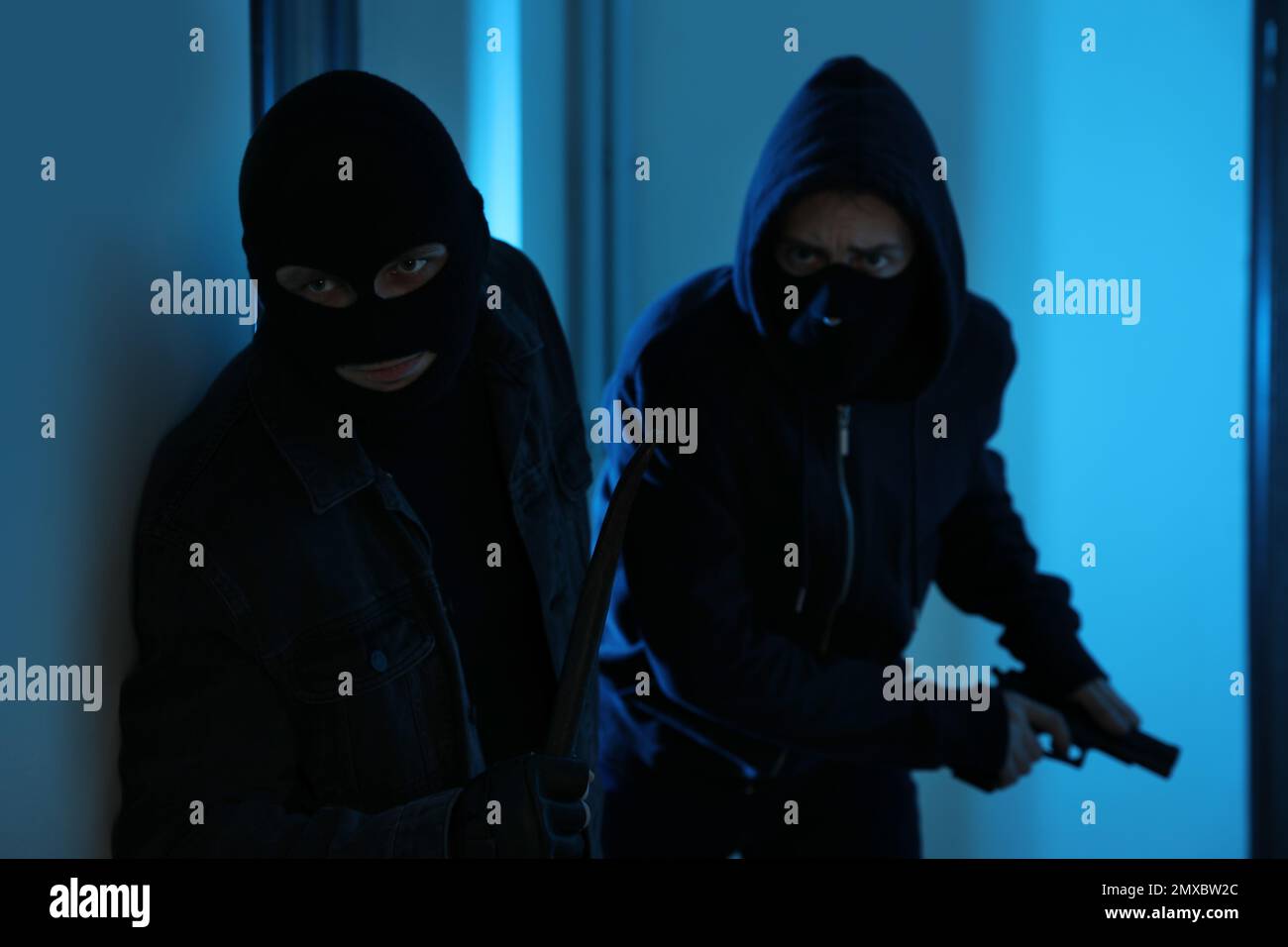 Dangerous criminals with gun and crow bar in hallway Stock Photo - Alamy