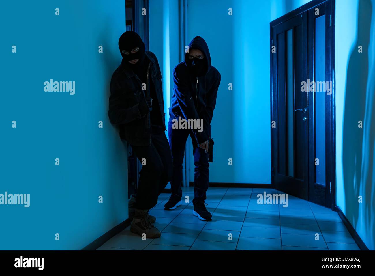 Dangerous criminals with gun and crow bar in hallway Stock Photo - Alamy