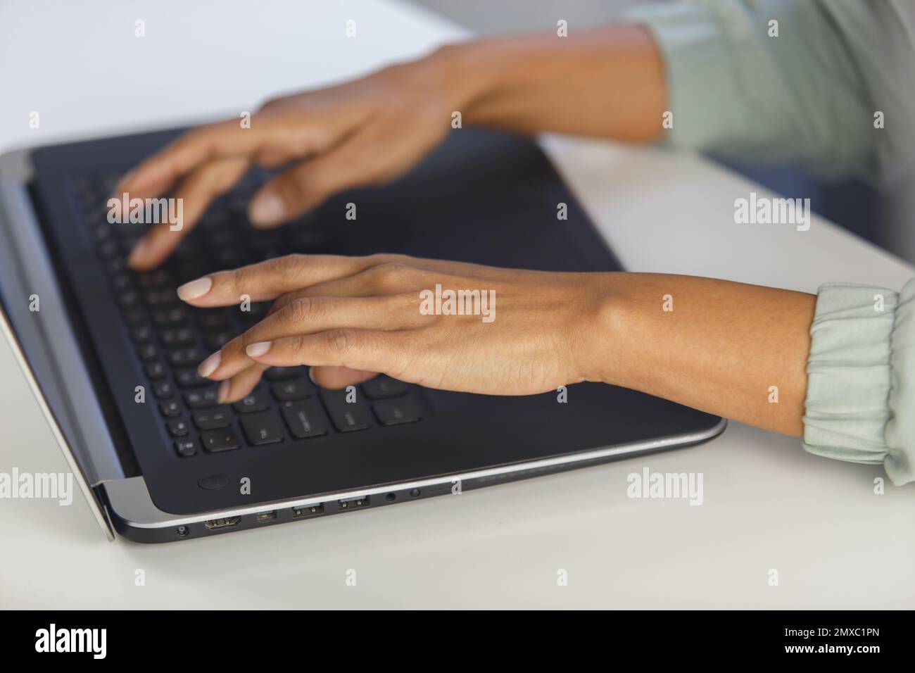Hands of young adult black woman working on laptop behind white desk in ...