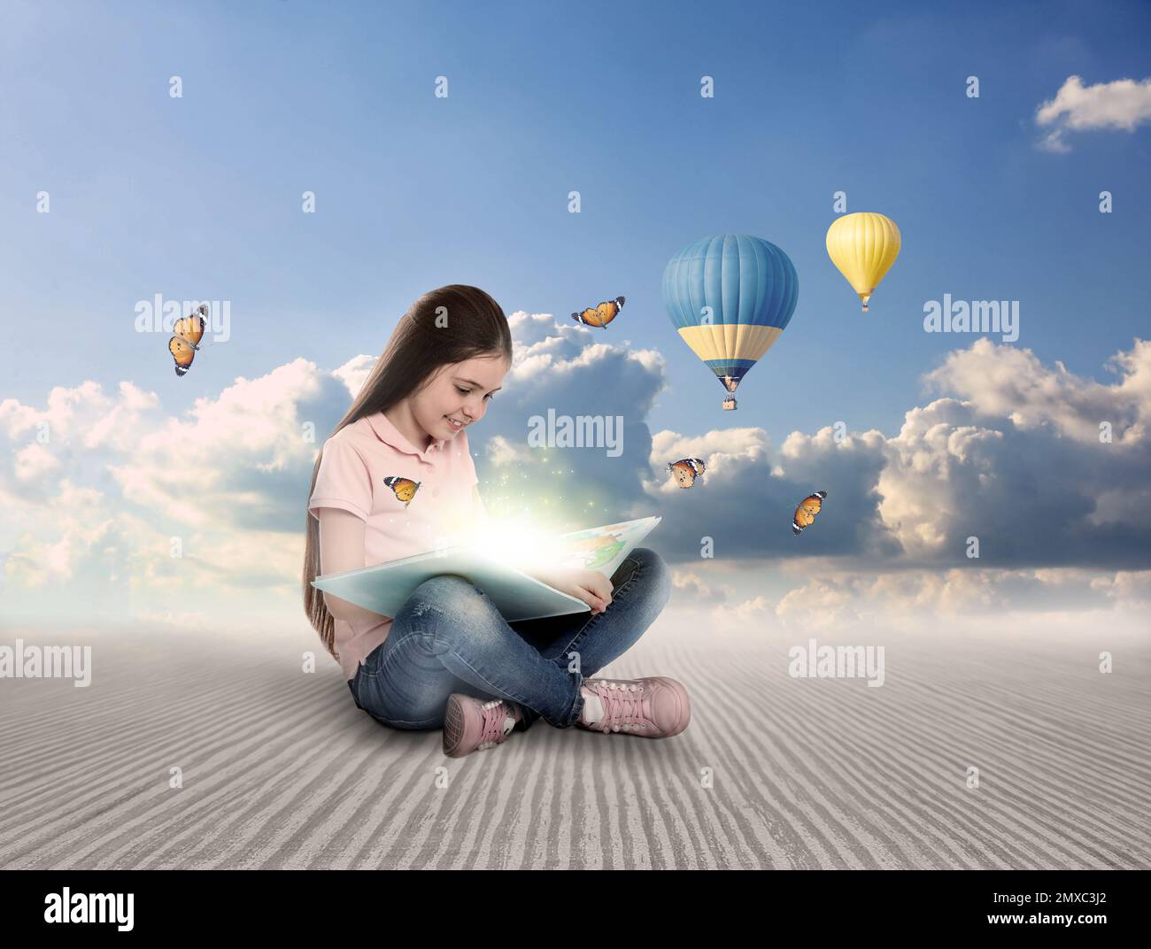 Cute little girl reading magic book. Picturesque view of blue sky and ...