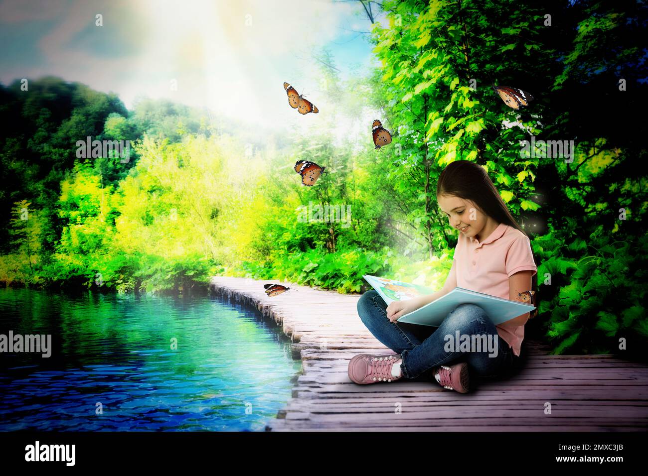 Cute little girl reading magic book on wooden bridge near lake Stock ...
