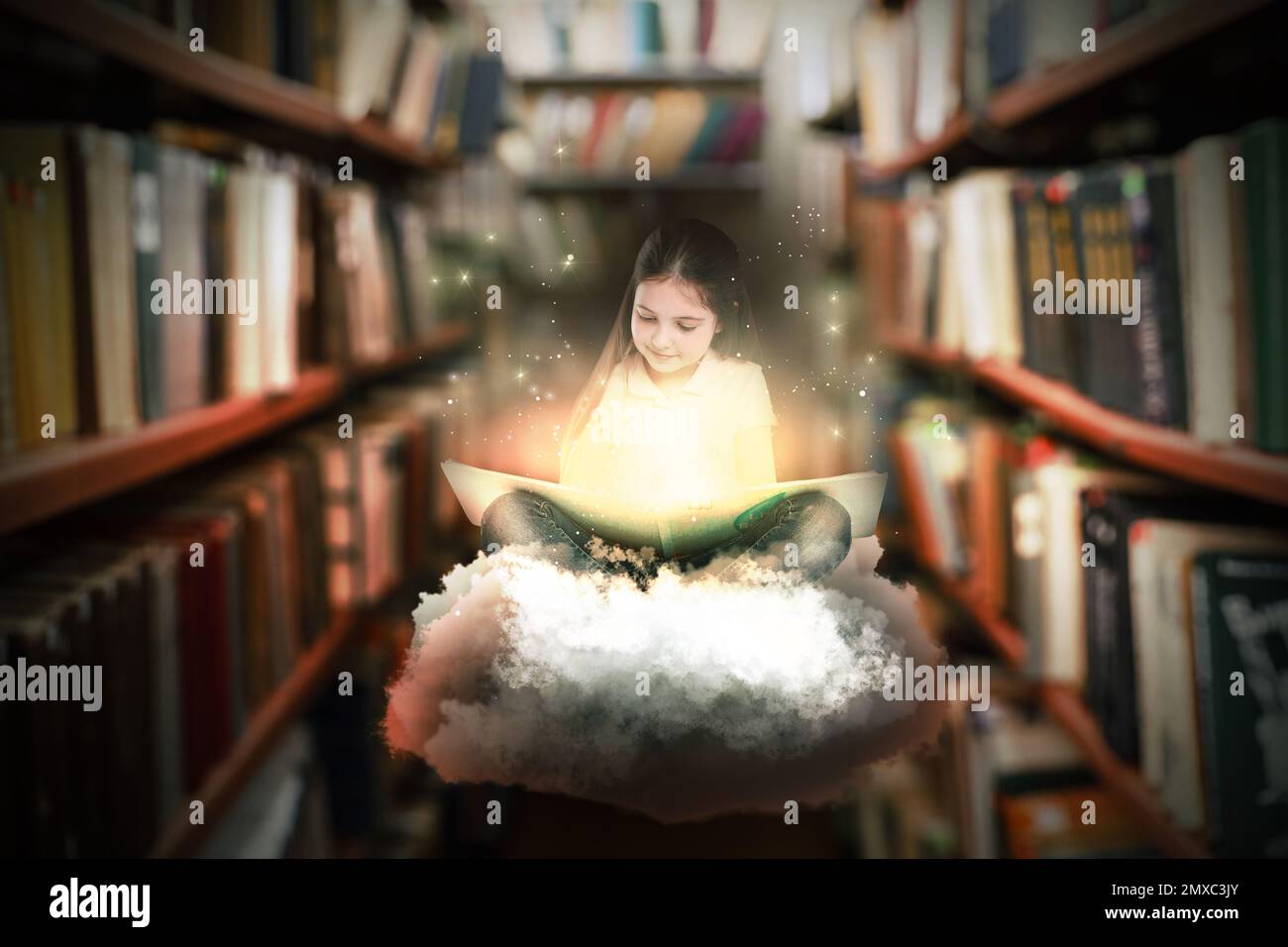 Cute little girl reading magic book in library Stock Photo - Alamy