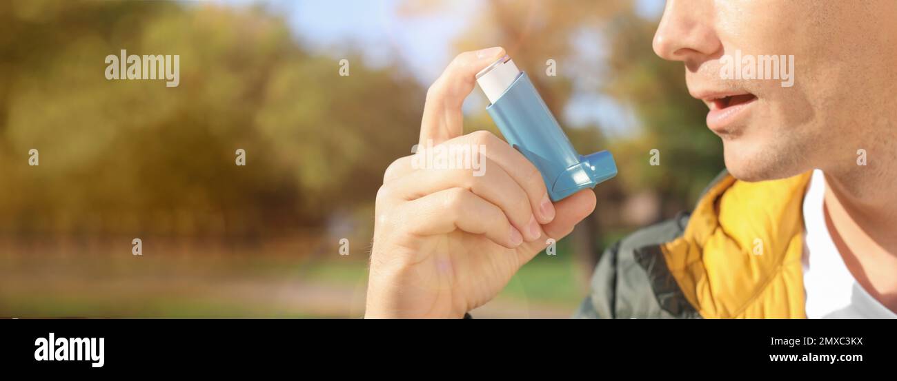Closeup view of man using asthma inhaler outdoors, space for text ...