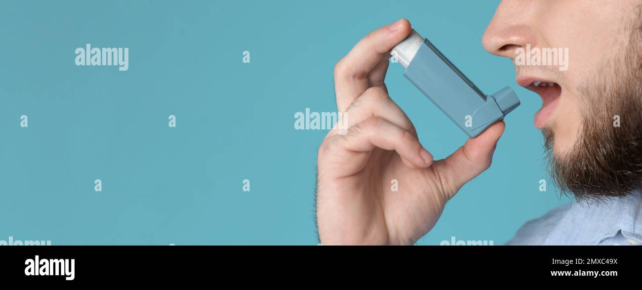 Closeup view of man using asthma inhaler on blue background, space for ...