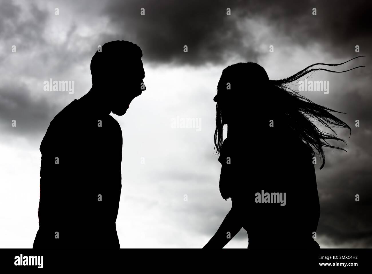 Silhouettes of arguing couple against sky with heavy rainy clouds ...