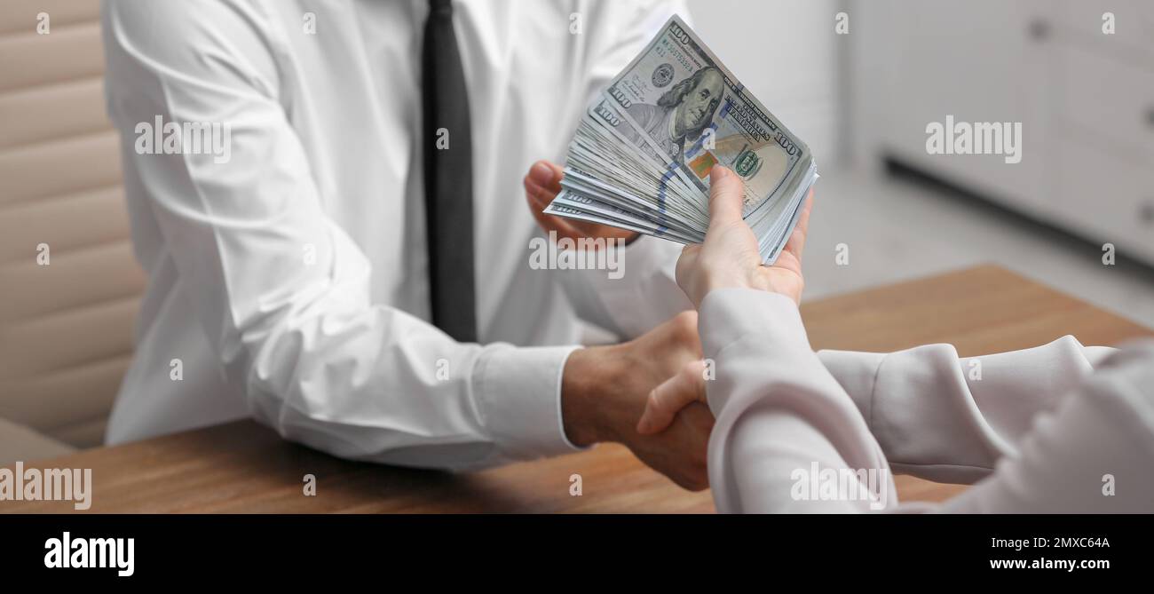 Woman shaking hands with man and offering bribe at table indoors ...
