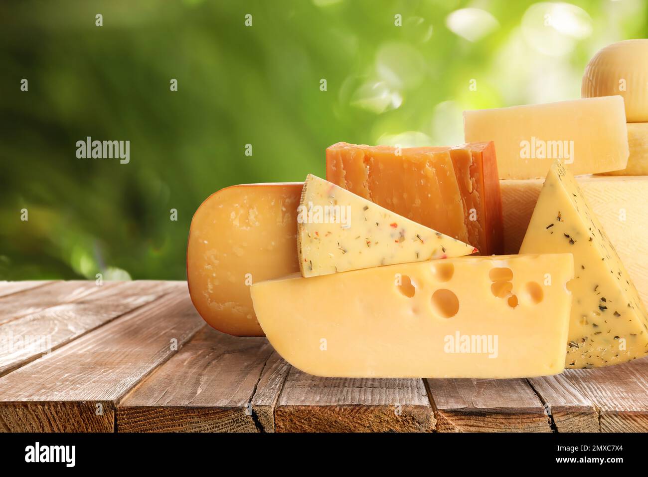 Different types of delicious cheeses on wooden table outdoors. Dairy ...