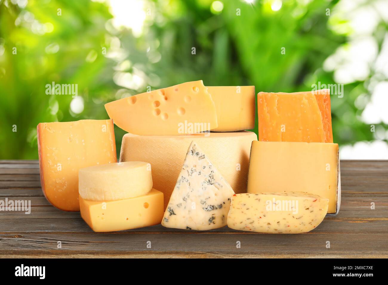 Different types of delicious cheeses on wooden table outdoors. Dairy ...
