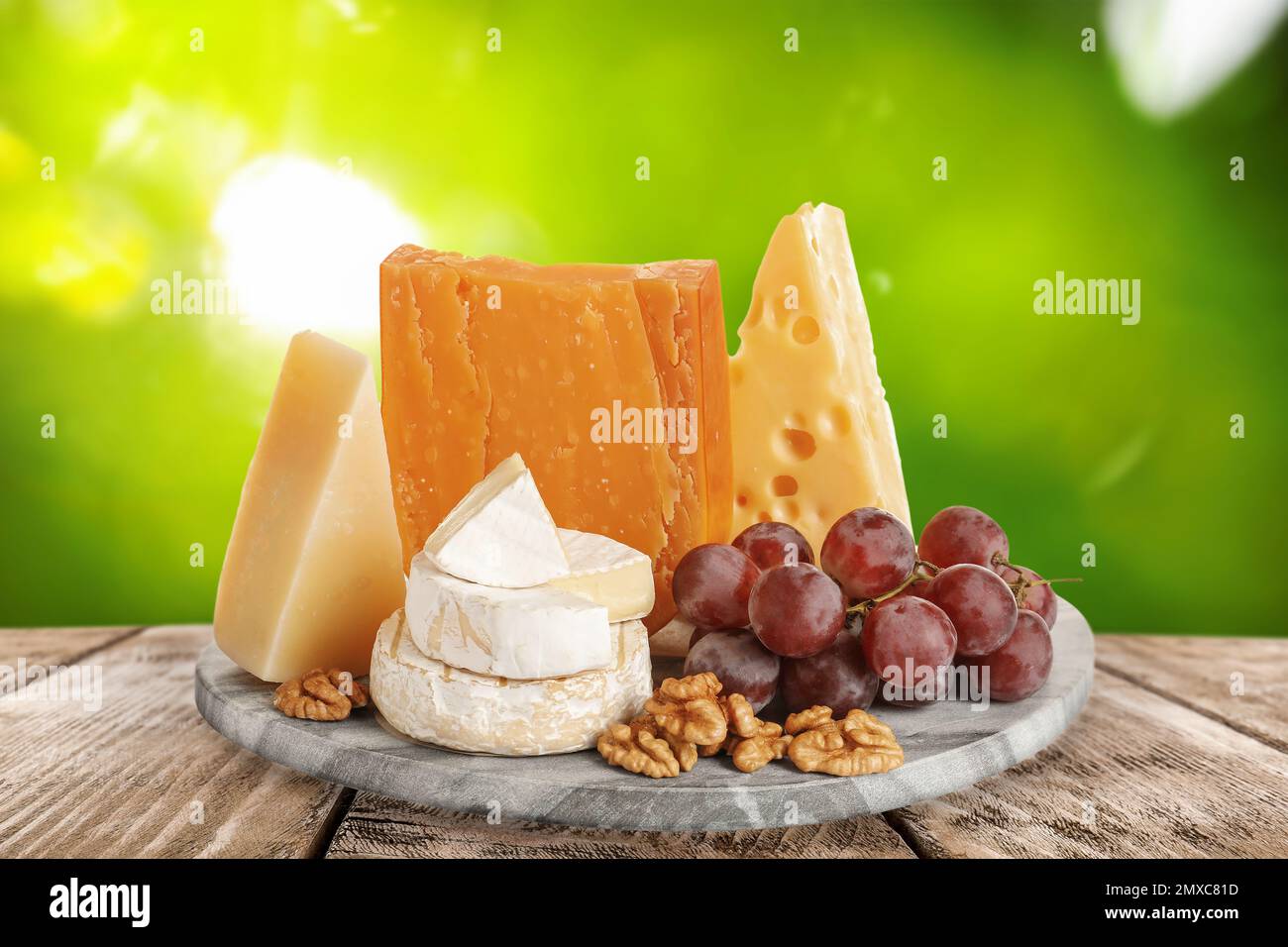 Different types of delicious cheeses on wooden table outdoors. Dairy ...