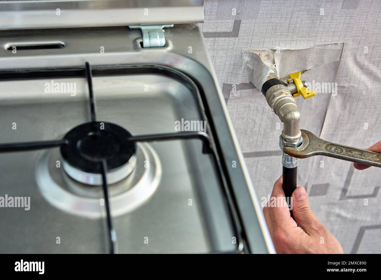 Disconnecting flexible hose from gas stove, gasman unscrews nut using ...