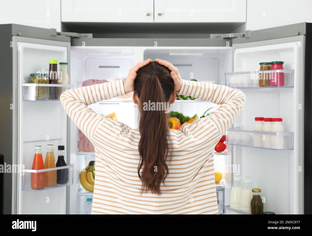 Worried young woman near open refrigerator in kitchen, back view Stock ...