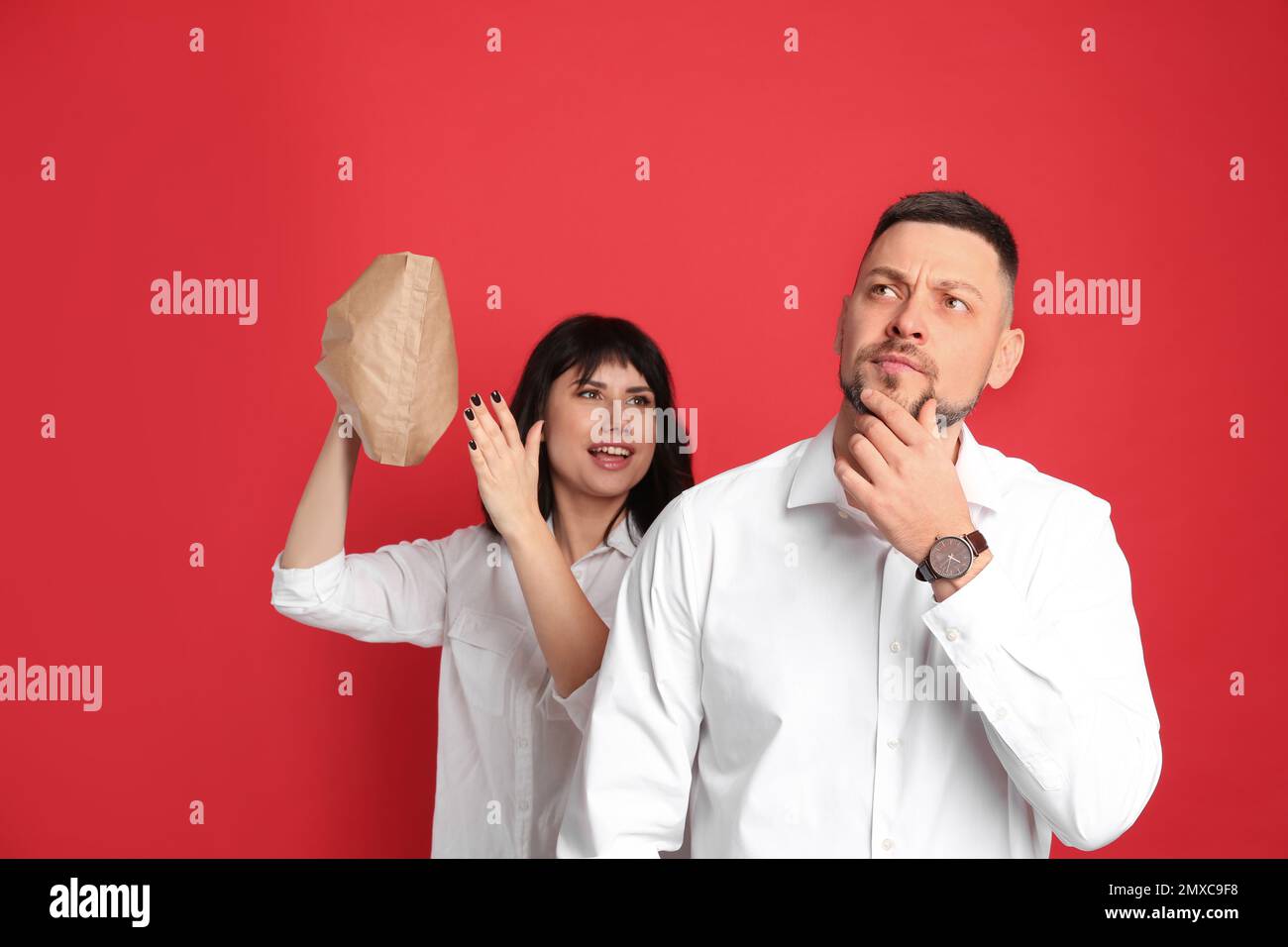 Woman popping paper bag behind her friend's back on red background ...