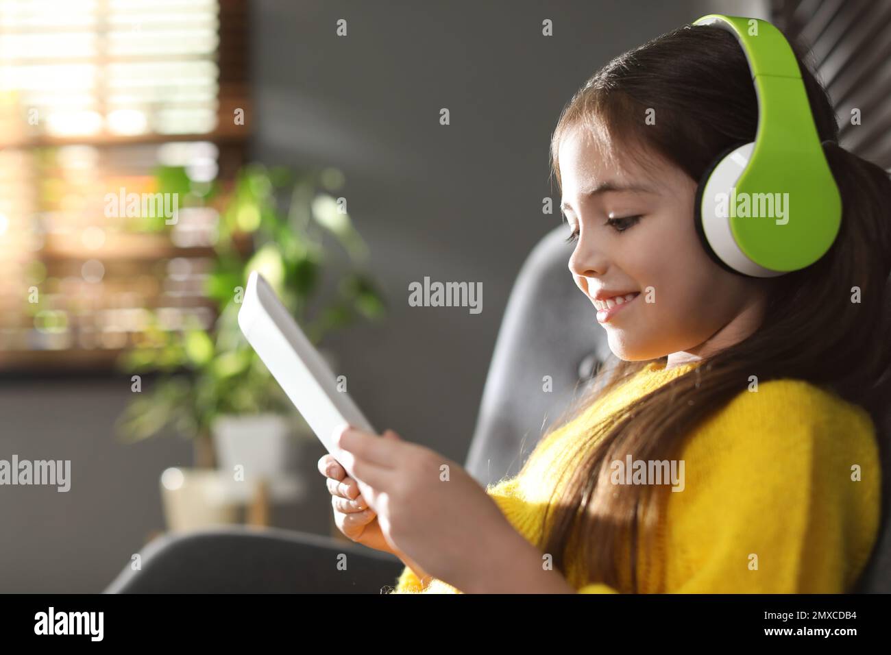 Cute little girl with headphones and tablet listening to audiobook at ...