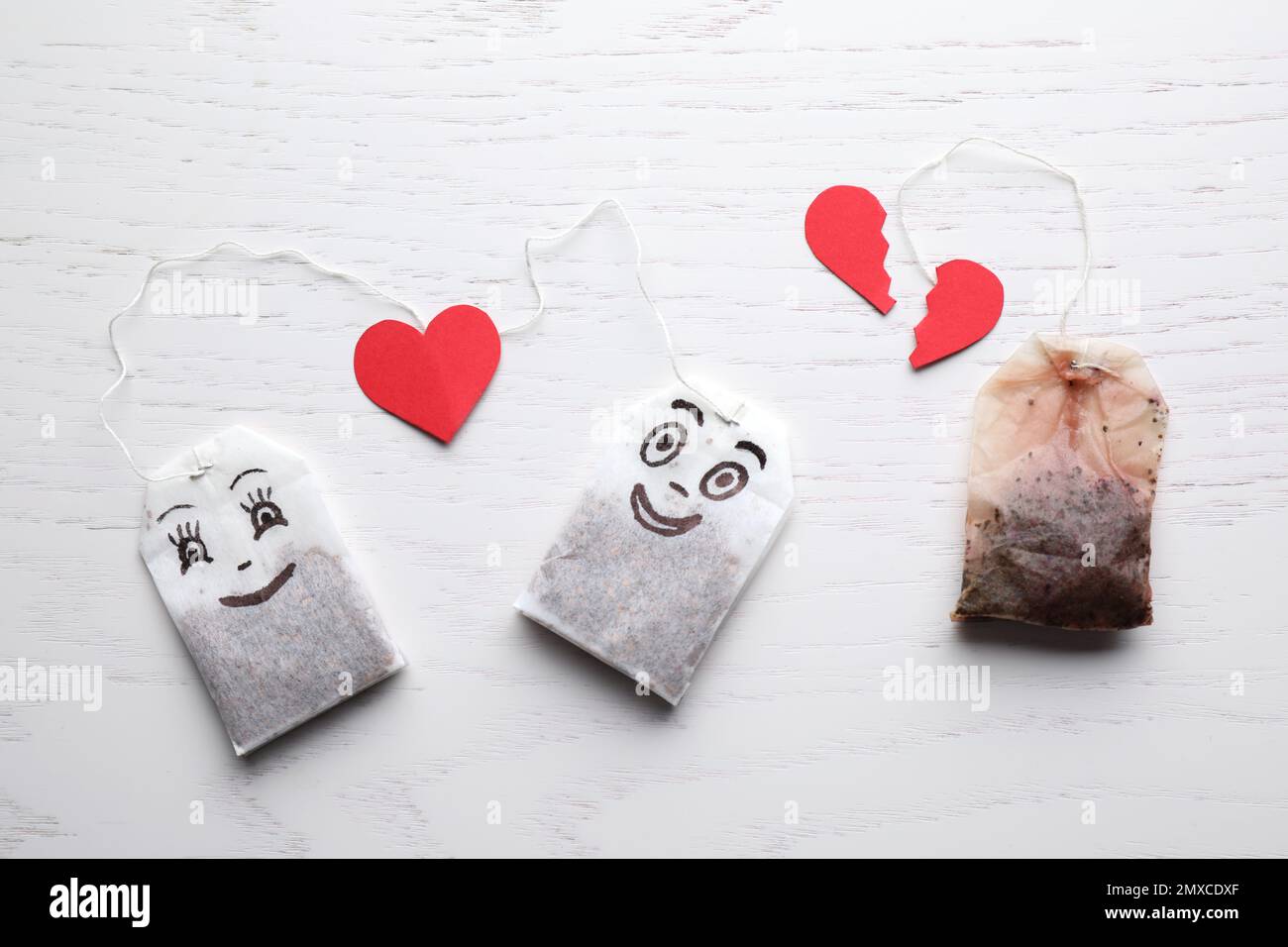Tea bags with drawn faces on white wooden background, flat lay. Concept ...