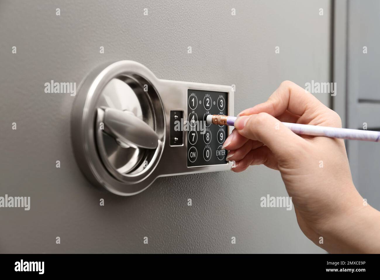 Woman using pencil to enter code on keypad of modern safe, closeup ...