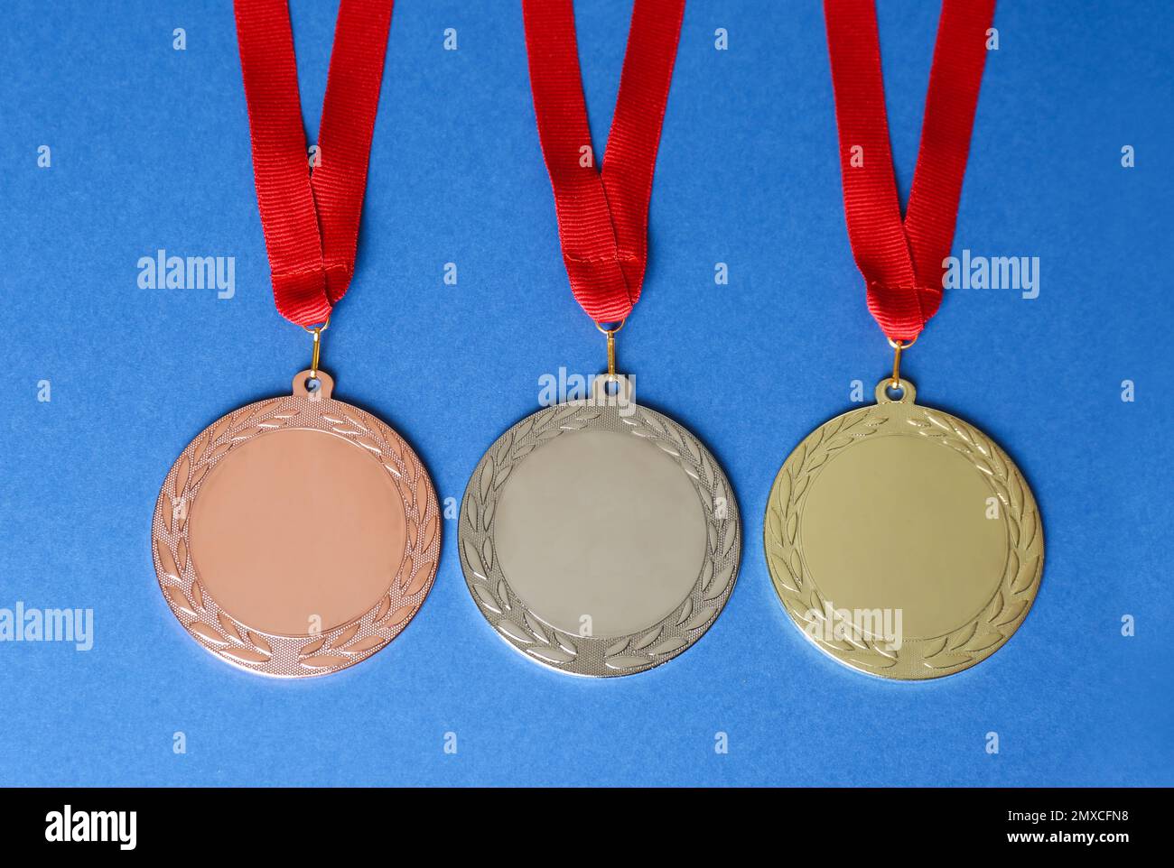 Gold, silver and bronze medals on blue background, flat lay. Space for ...